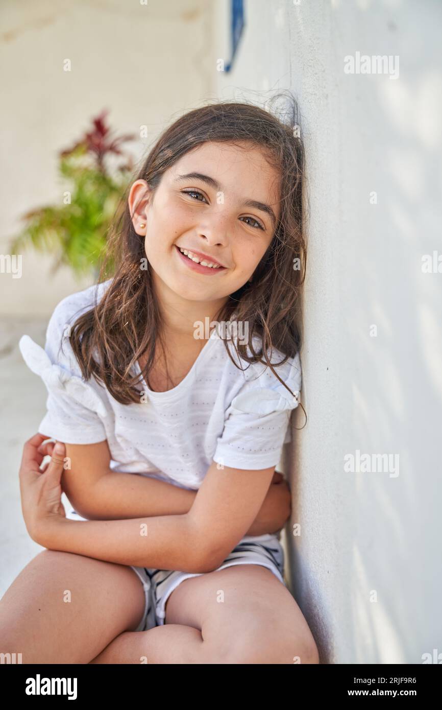 Adorable cheerful preteen girl in t shirt and shorts sitting on street ...
