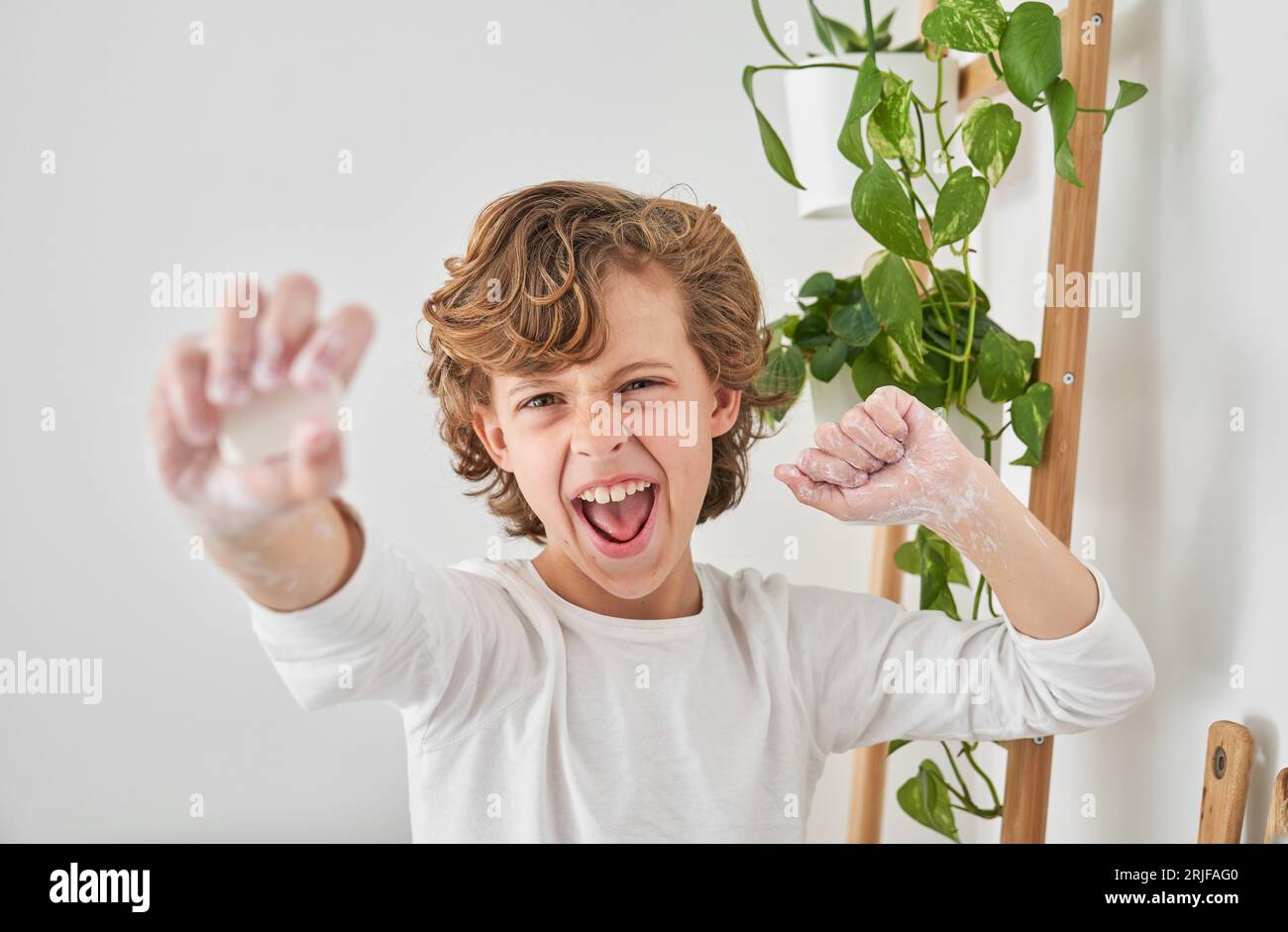 Joyful boy with curly hair washing hands with soap and reaching arm to ...