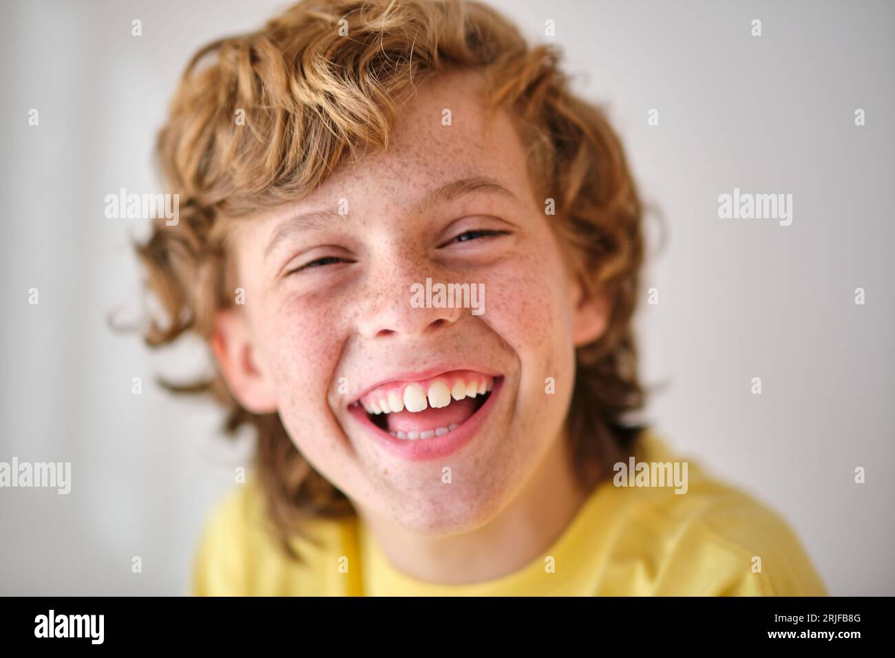 Smiling kid in yellow outfit with brown wavy hair looking at camera in ...