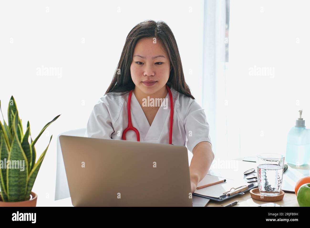 Concentrated Asian female therapist in medical uniform browsing modern ...