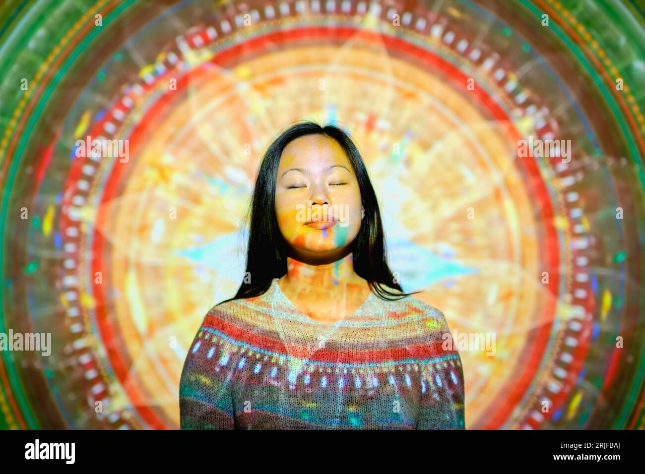 Tranquil Asian female with light on face and closed eyes standing near ...