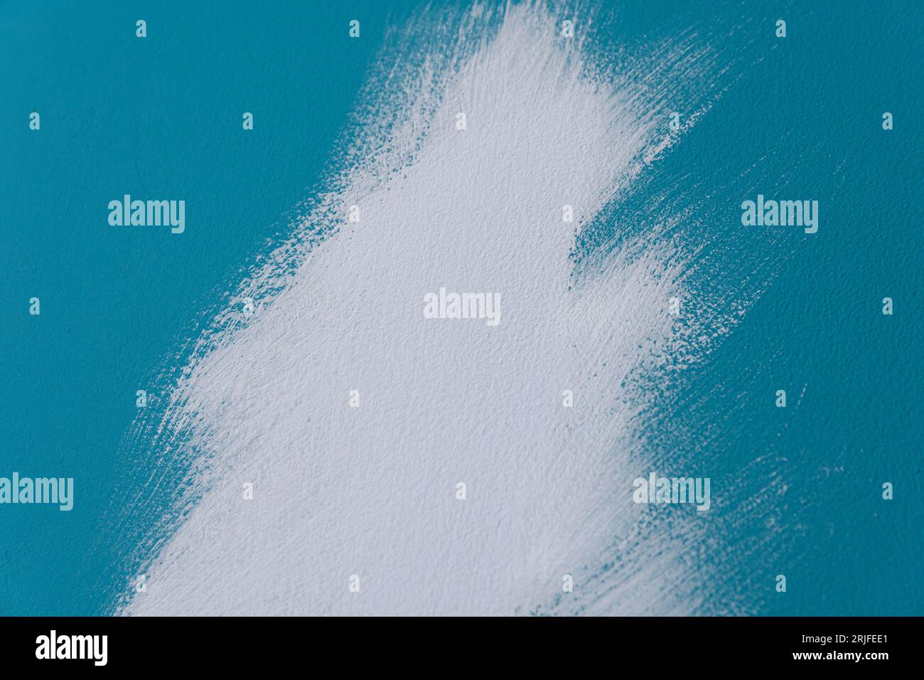 Close up of smear of white paint with a paint brush on a blue wall ...