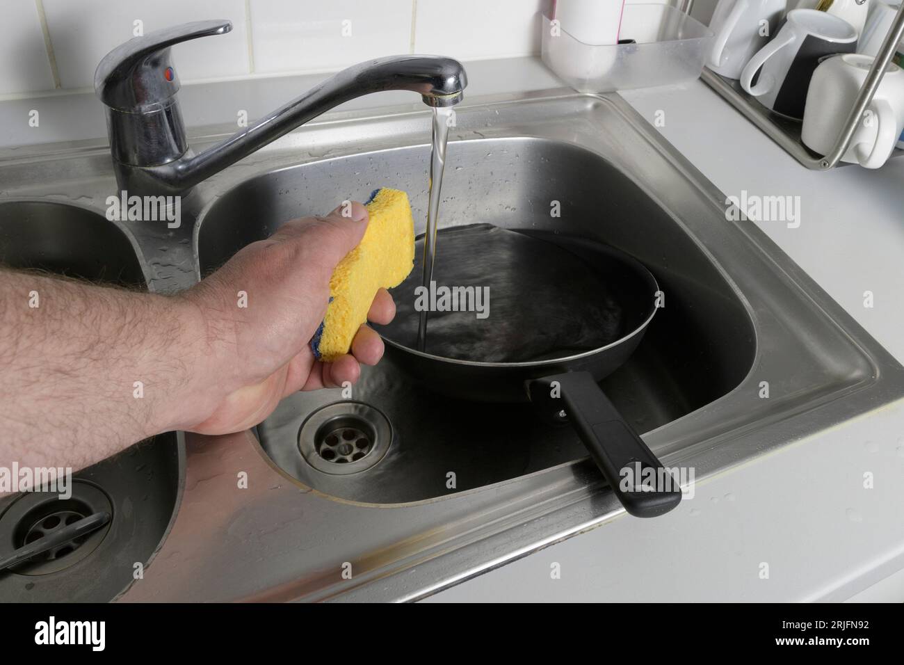 A man's hand washes a frying pan in the kitchen under a tap with ...