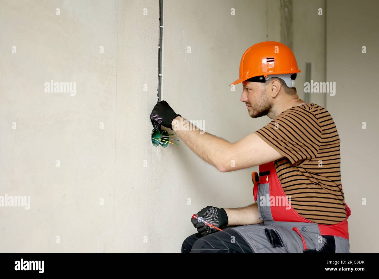 Electrician male in uniform, protective gloves and helmet checks ...