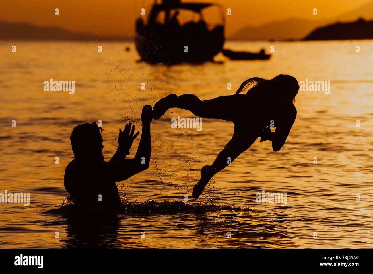 A brother and sister enjoy playful moments in the sea during sunset ...