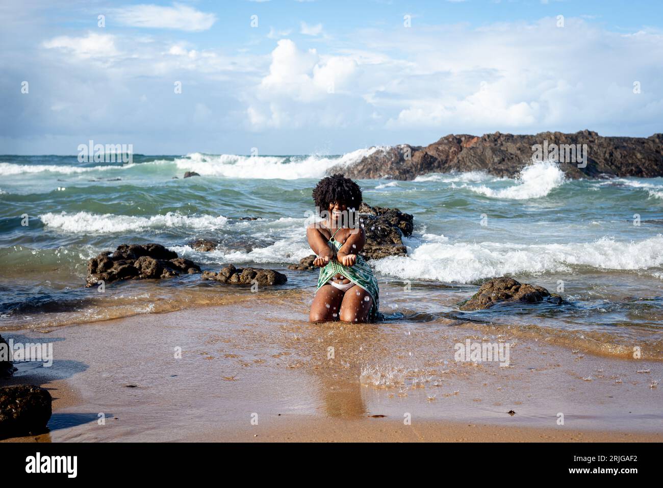 Portrait of beautiful woman with black power hair kneeling on beach ...