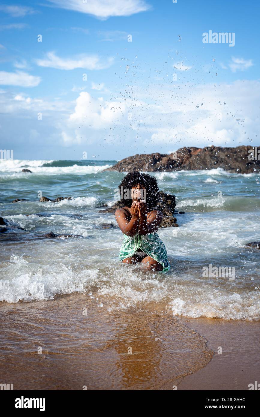 Portrait of beautiful woman with black power hair kneeling on beach ...