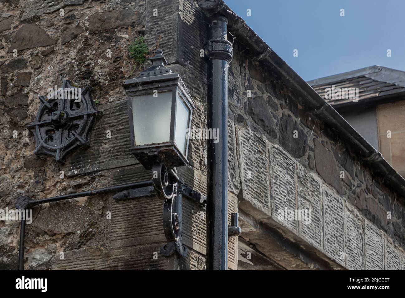 Old drain pipe and carriage light attached to a wall painted black ...