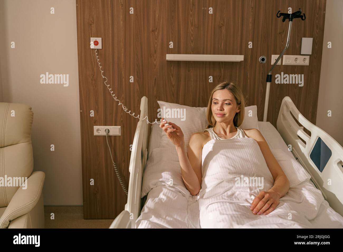 Young smiling woman patient holding emergency call button while lying ...