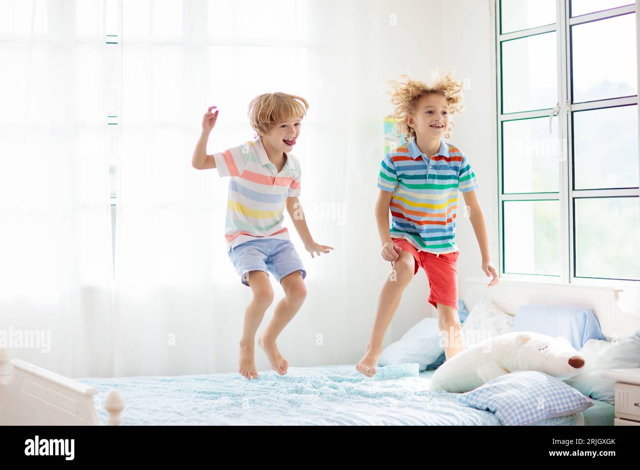 Child jumping on bed in white bedroom with big window. Kids play at ...