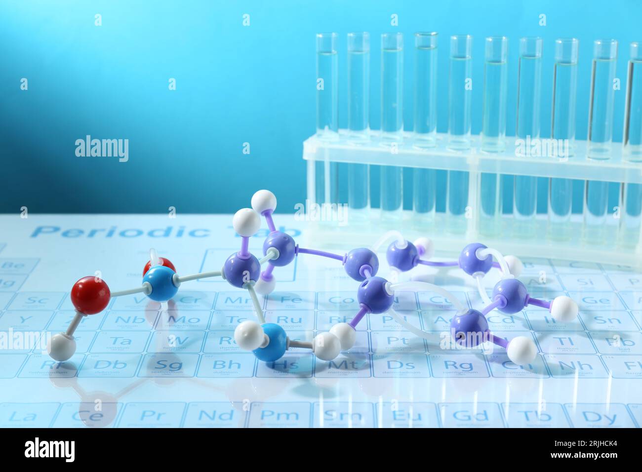 Molecular model and test tubes on periodic table against light blue ...