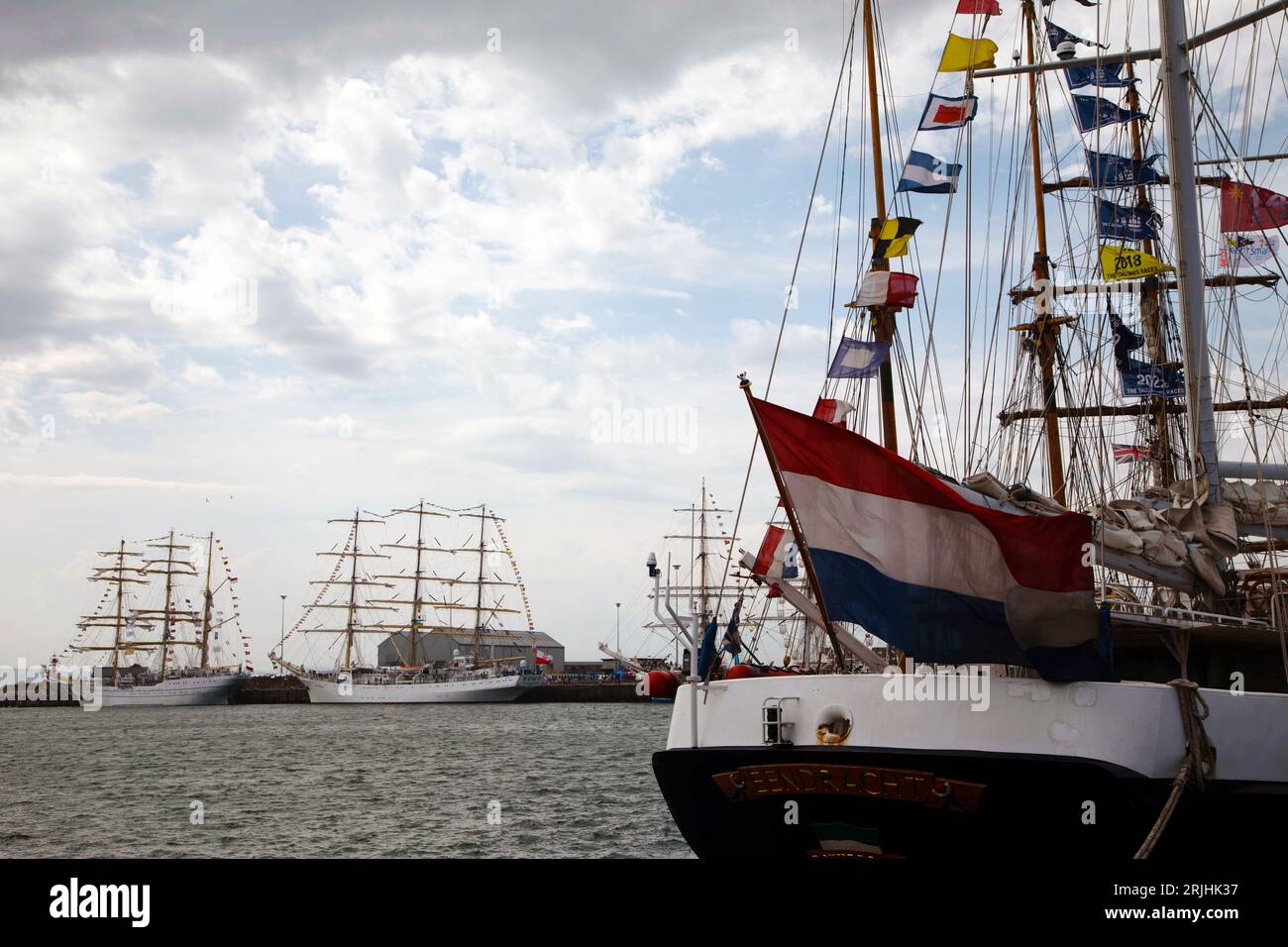 A fleet of tall sailing vessels docked on the tranquil blue waters of ...