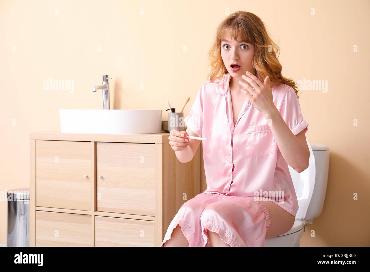 Shocked Young Woman With Pregnancy Test Sitting On Toilet Bowl In