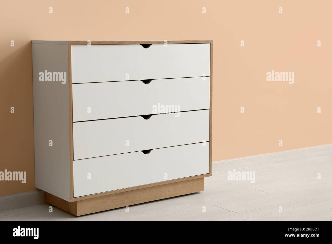 Light wooden chest of drawers near beige wall Stock Photo - Alamy