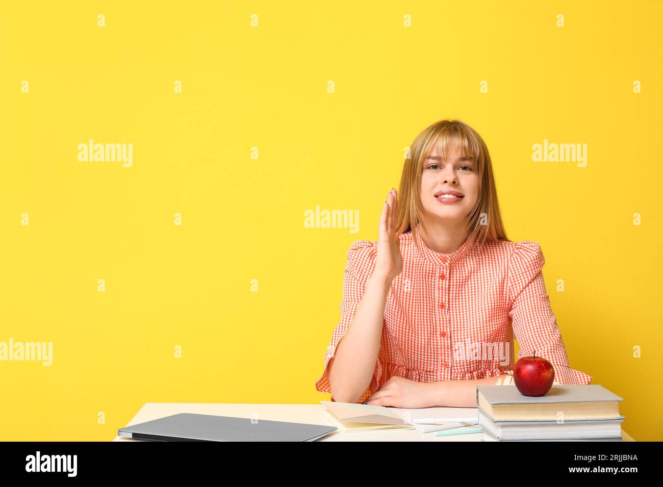 Female student raising hand at table on yellow background Stock Photo ...
