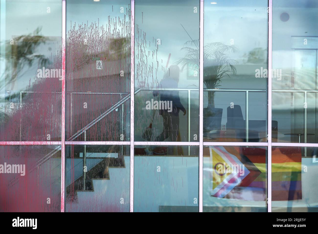 A silhouetted figure carries a mop behind smoked glass windows with red ...