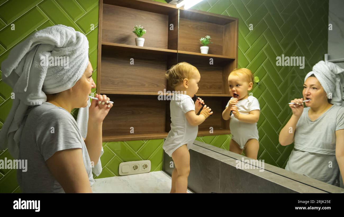 Female person and child brush teeth looking in large mirror Stock Photo ...