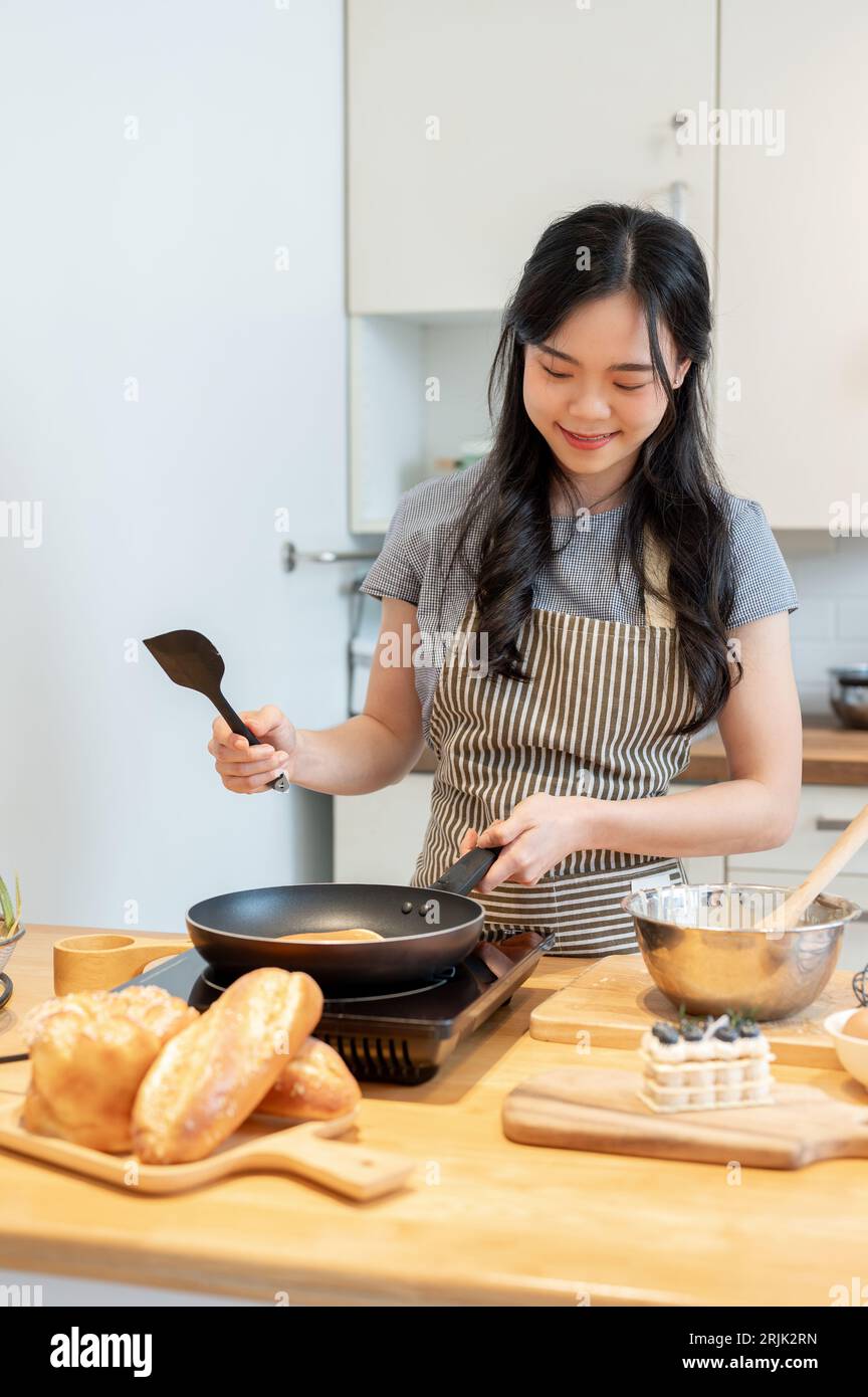 A portrait of a lovely young Asian woman in an apron cooking pancakes ...