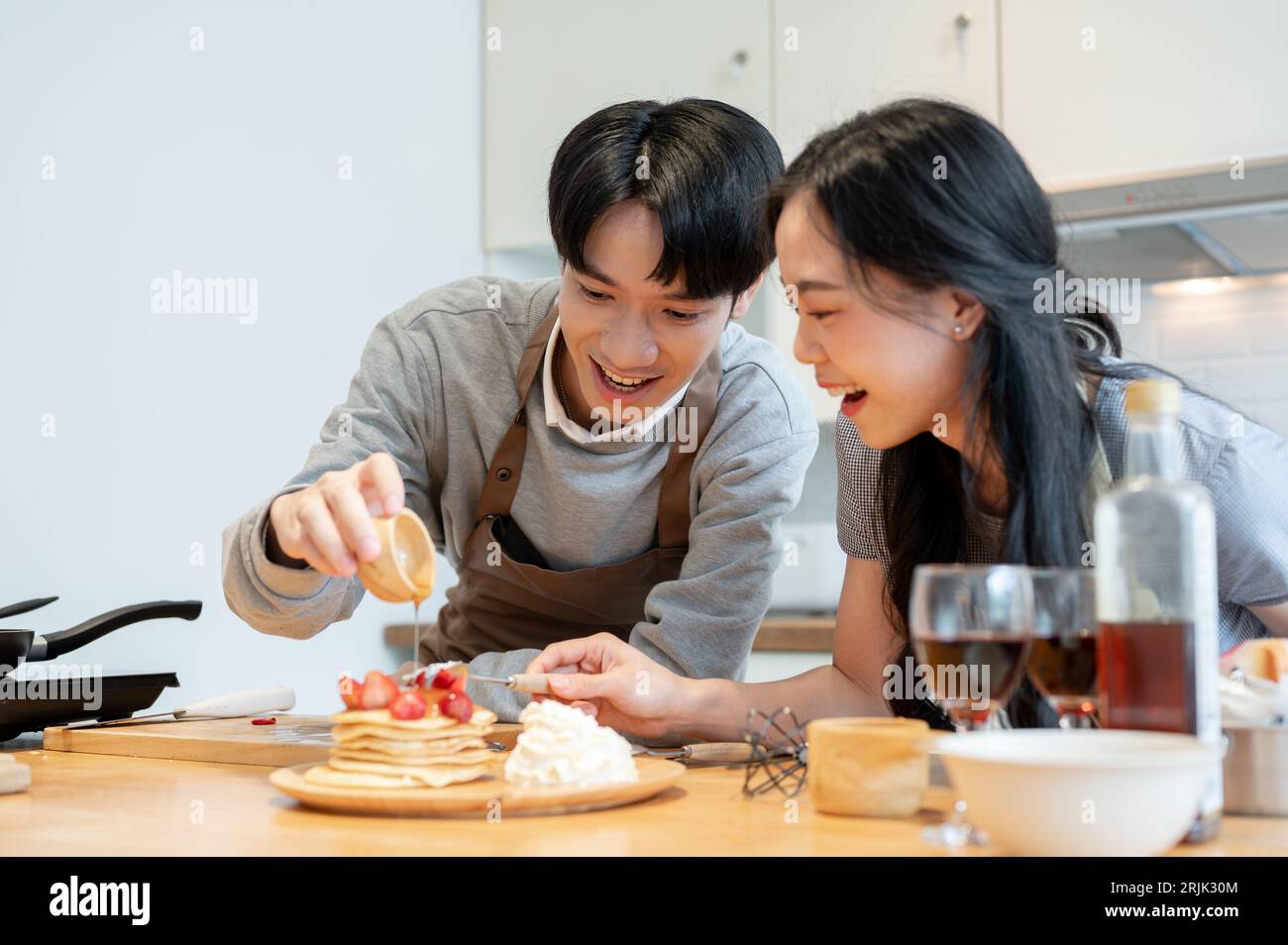 A handsome young Asian man is pouring syrup or honey on pancakes ...