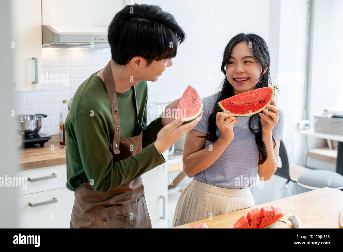 A lovely Asian couple enjoys eating watermelon together in the kitchen ...