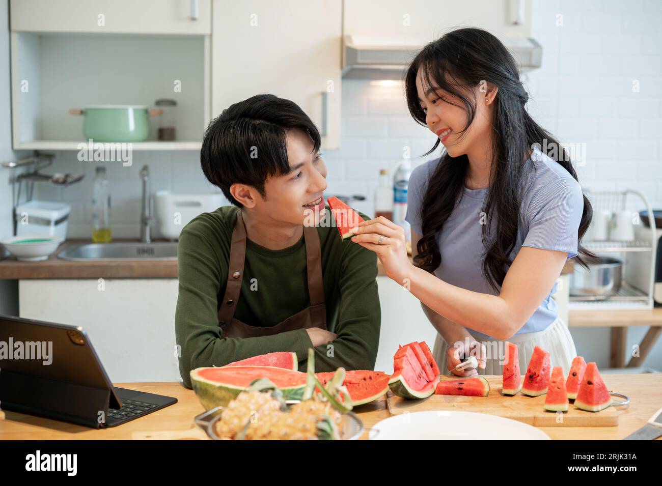 A happy and handsome young Asian man is being fed a slice of watermelon ...