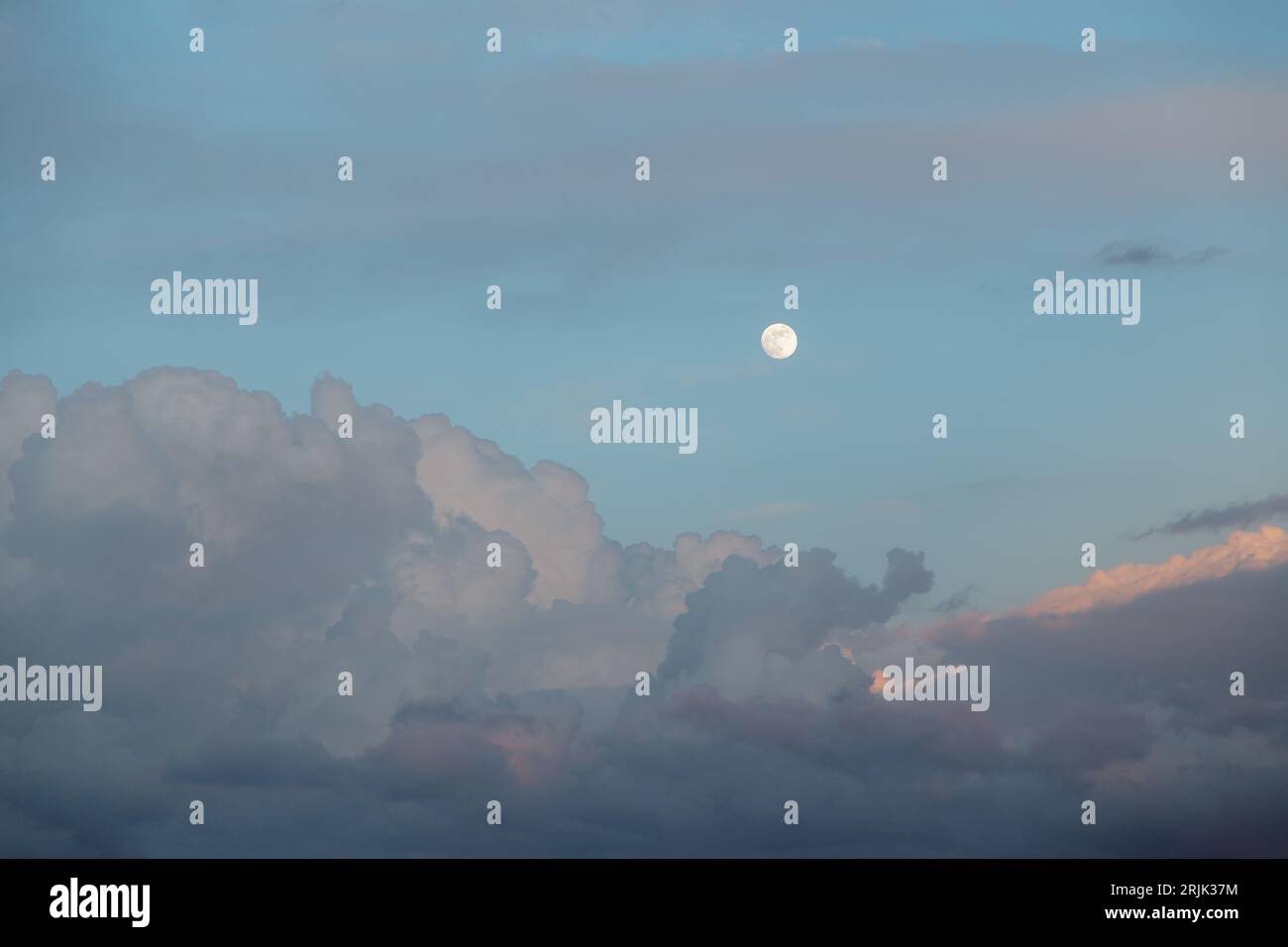 Horizontal shot cumulus clouds float across the evening sky with a full ...