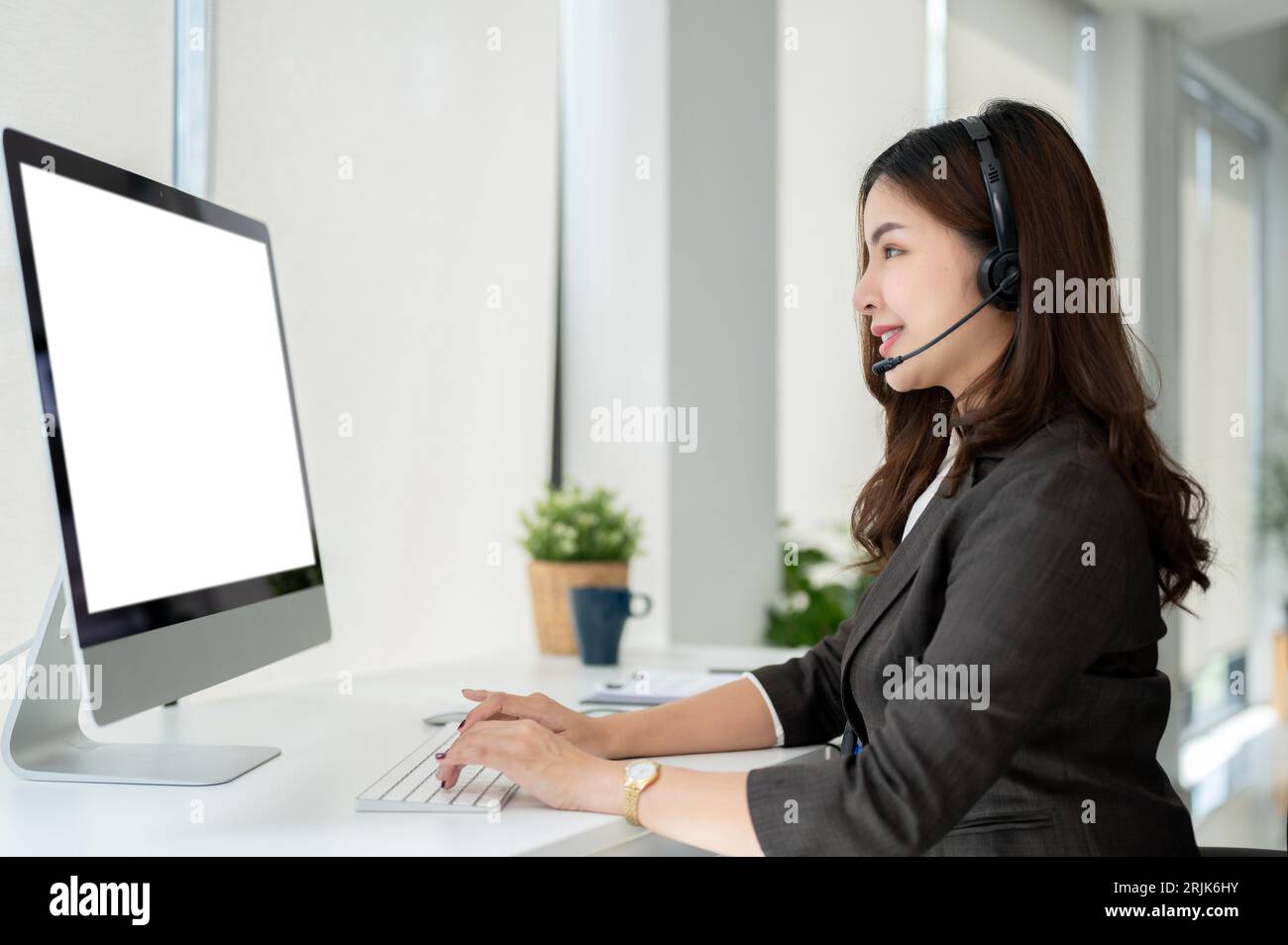 A professional and beautiful Asian female customer support agent is looking at her computer ...