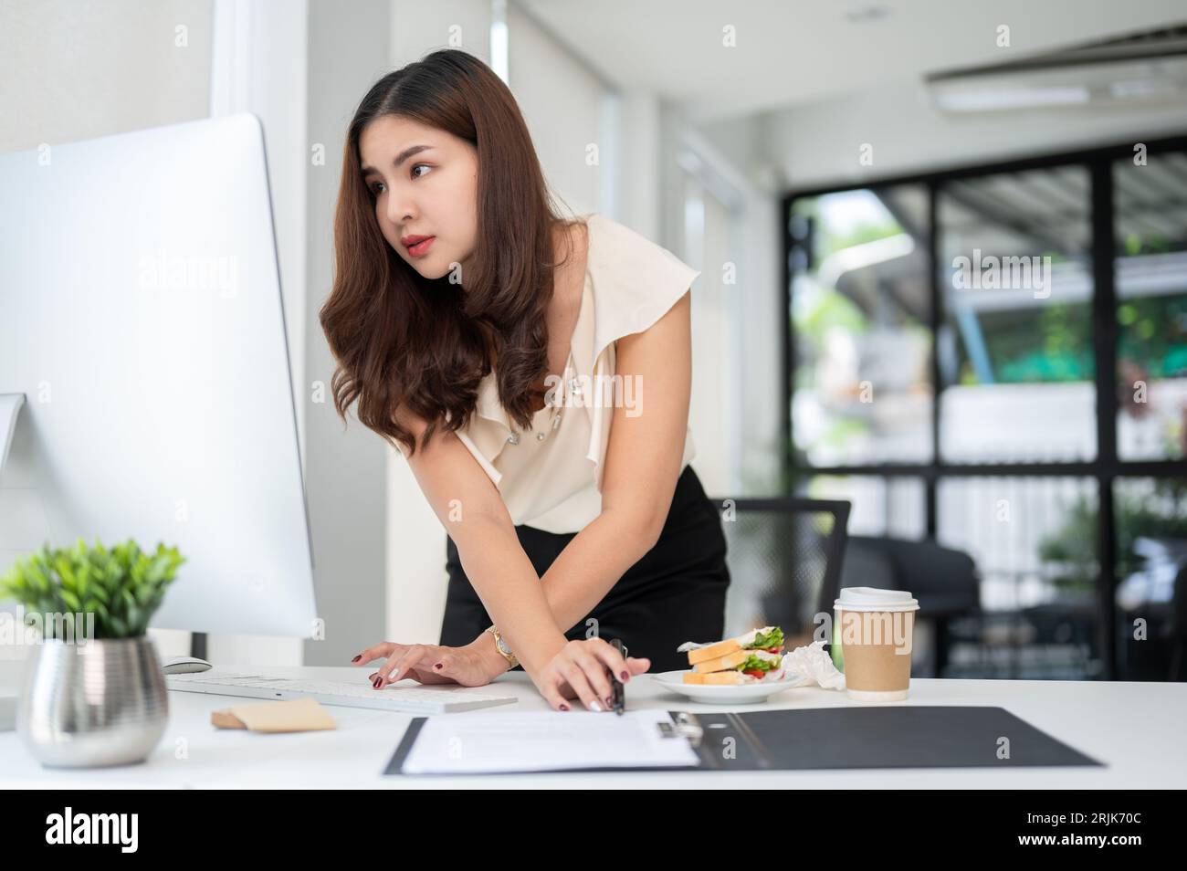 A professional and focused Asian businesswoman is bending over a table ...