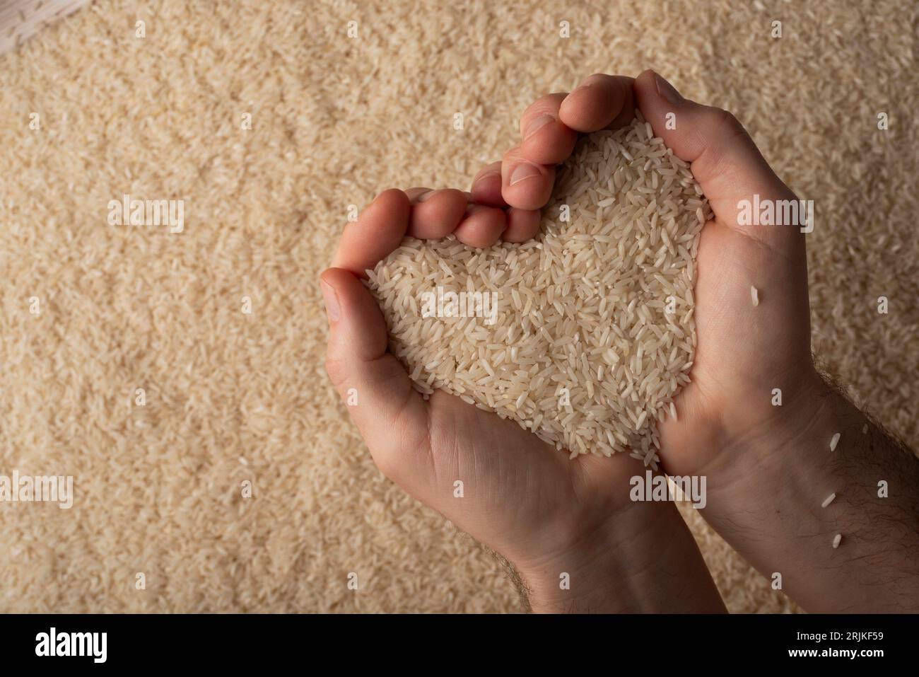 Human hands in shape of heart holding handful of rice on rice ...