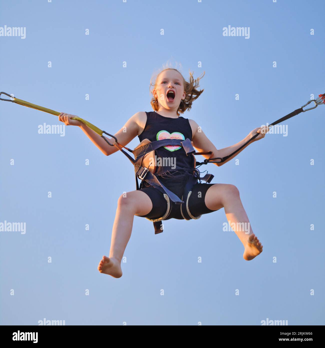 Little white girl child jumping on a trampoline with insurance elastic bands in an amusement ...