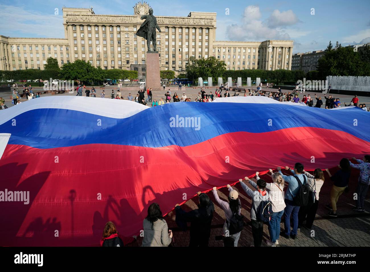 Volunteers hold a giant Russian national flag next to a statue of ...
