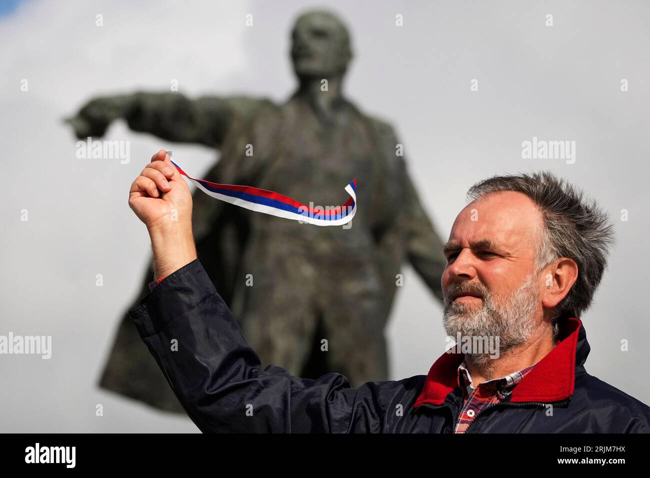 A man waves with a ribbon in colours of Russian flag next to a statue ...