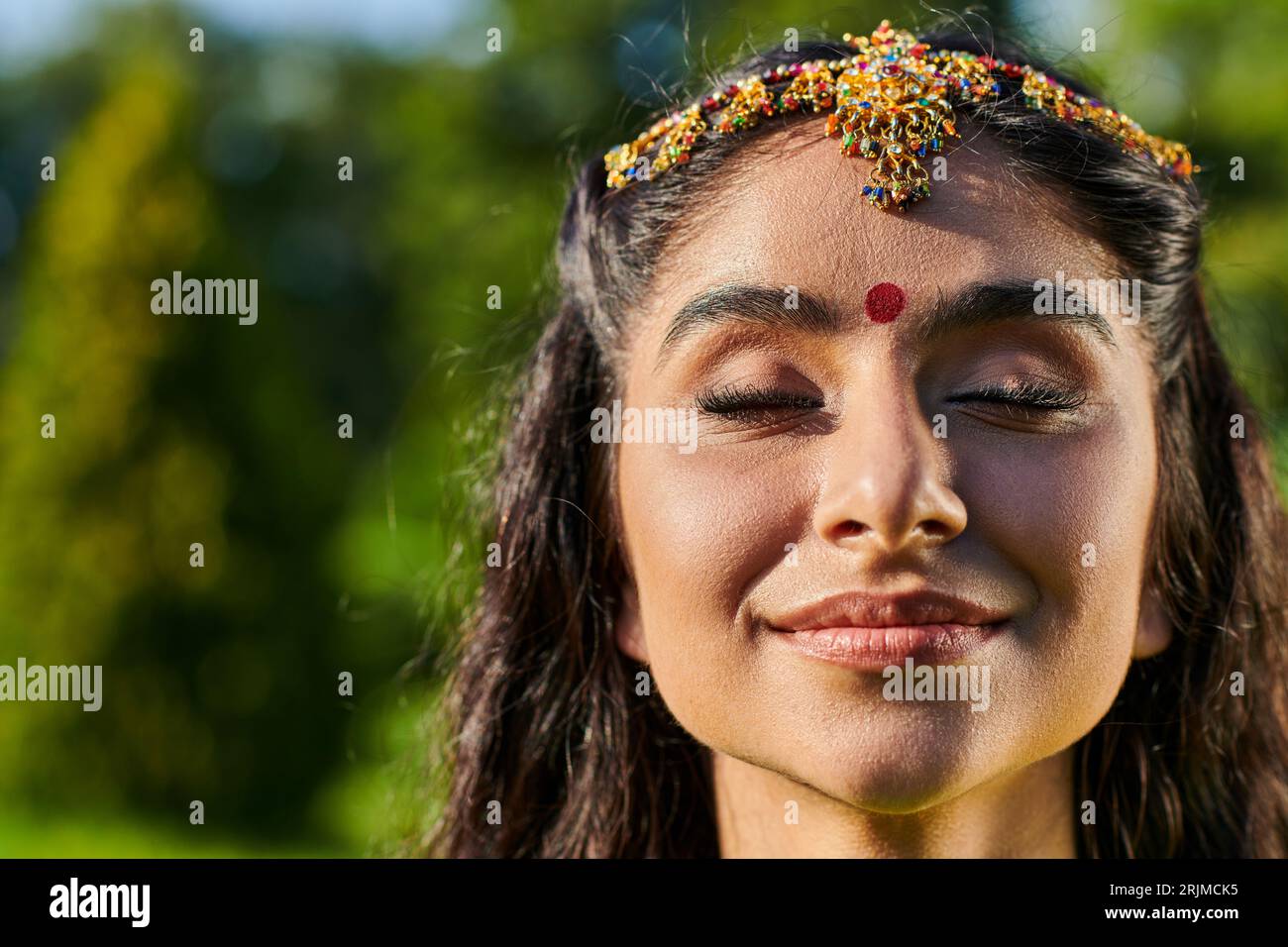 portrait of smiling indian woman with bindi and matha patti standing ...
