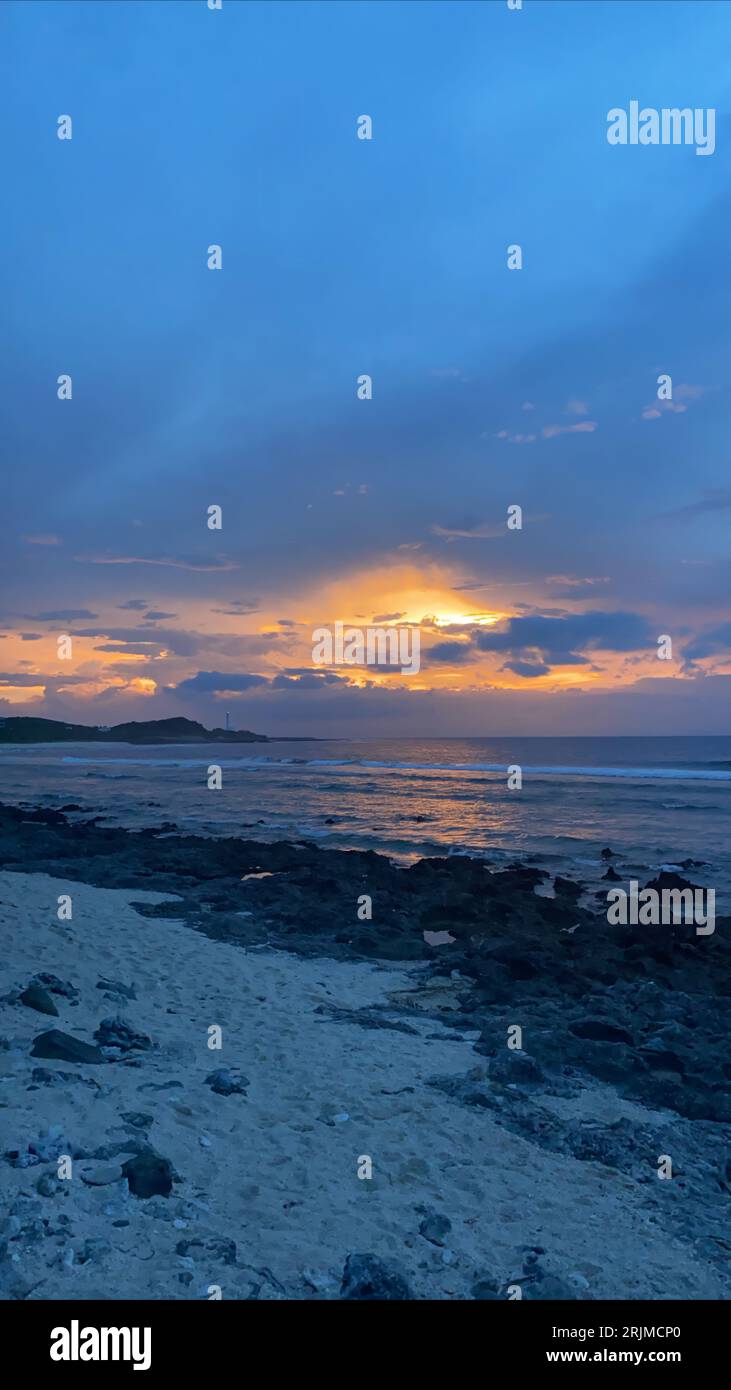A tranquil beach scene at sunrise, with the still ocean stretching out ...