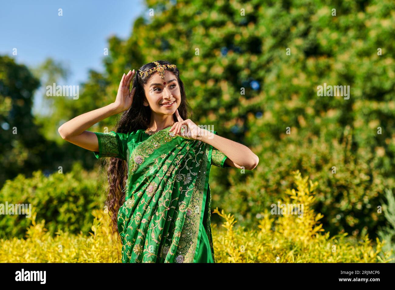 trendy young indian woman in traditional outfit and bindi posing near ...