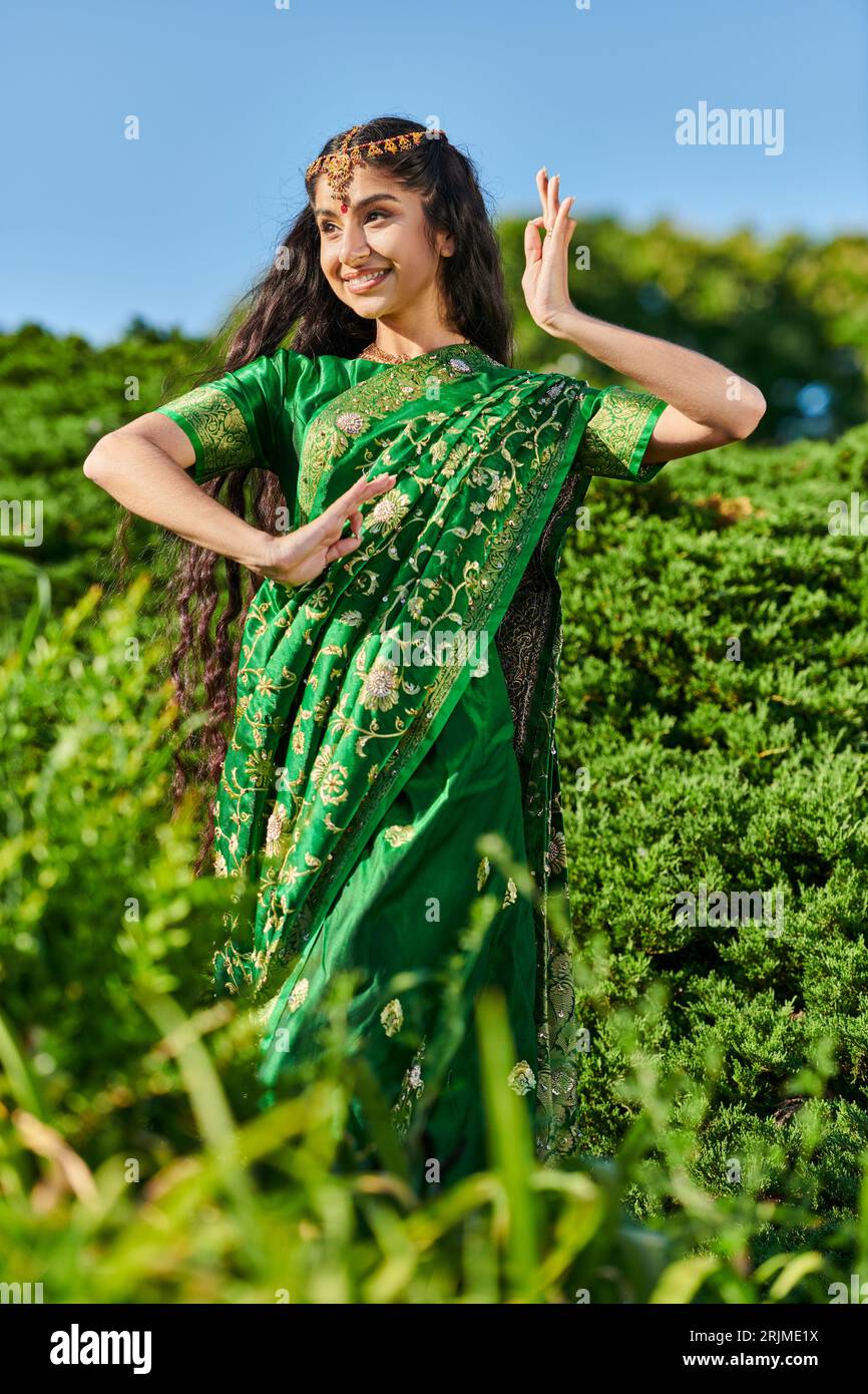carefree young indian woman in traditional sari dancing while standing ...