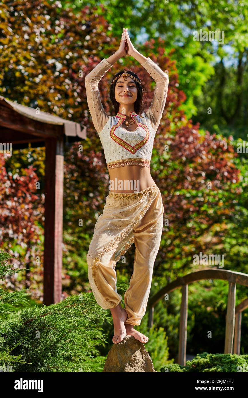 joyful indian woman in elegant ethnic wear standing with raised praying ...