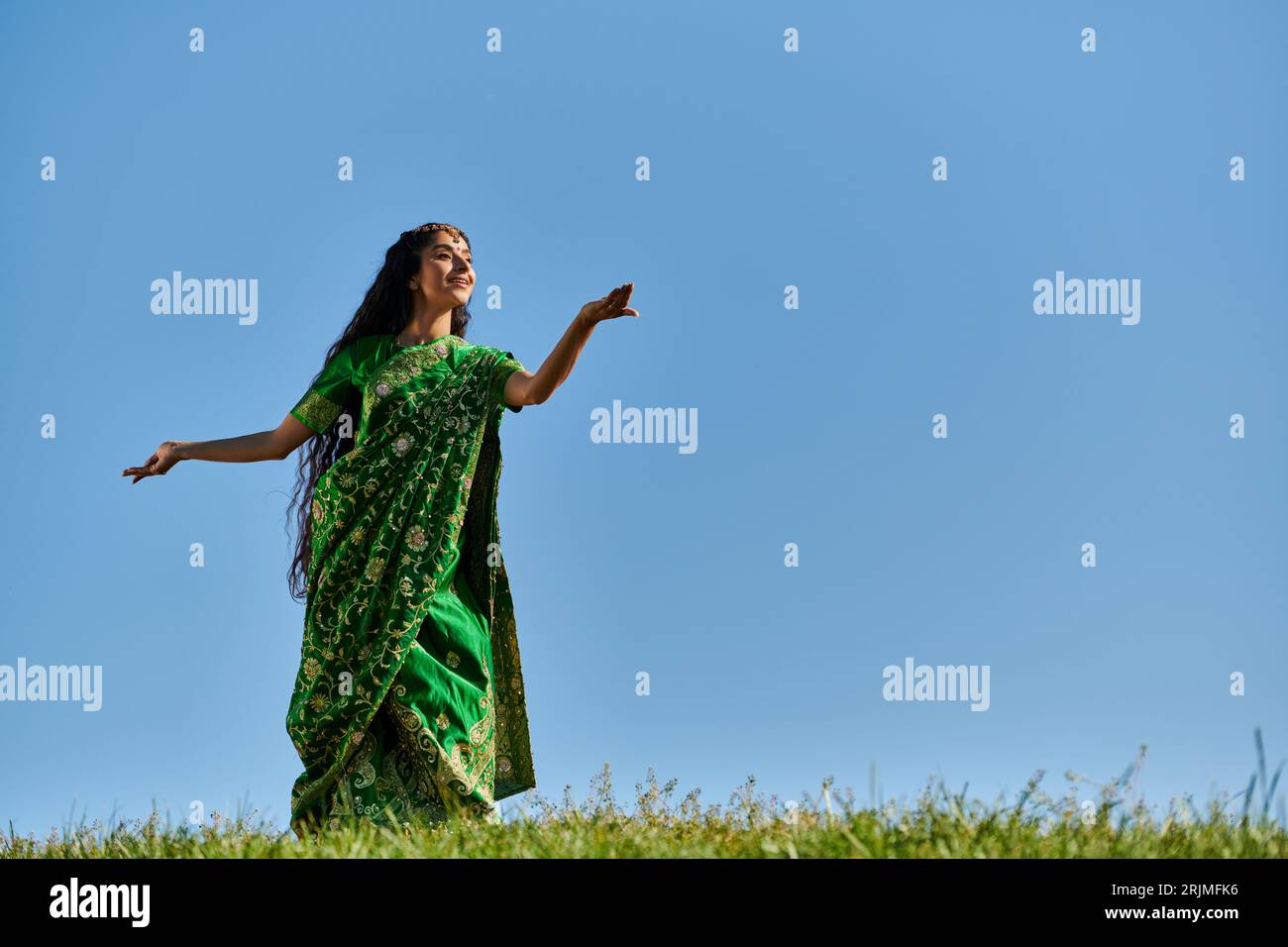 elegant indian woman in traditional sari dancing on green meadow under ...