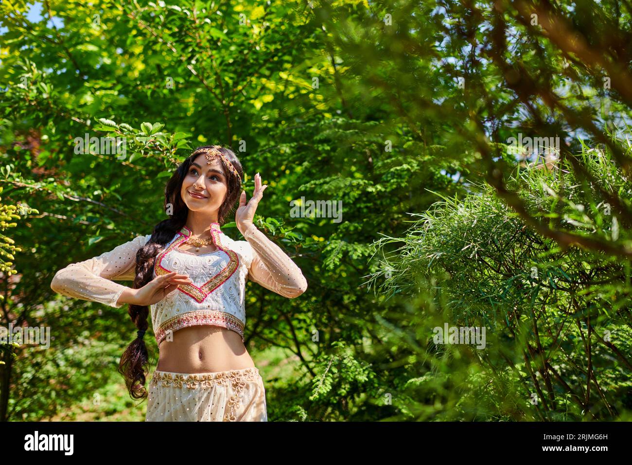 young and happy indian woman in traditional attire dancing during park ...