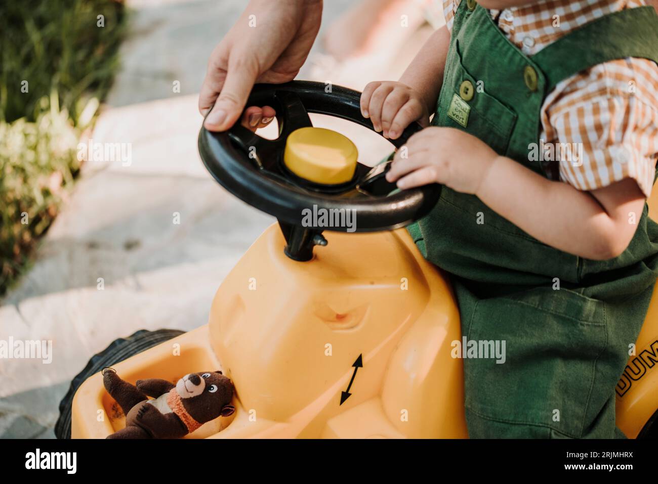 A young child driving a toy tractor under the watchful supervision of a ...
