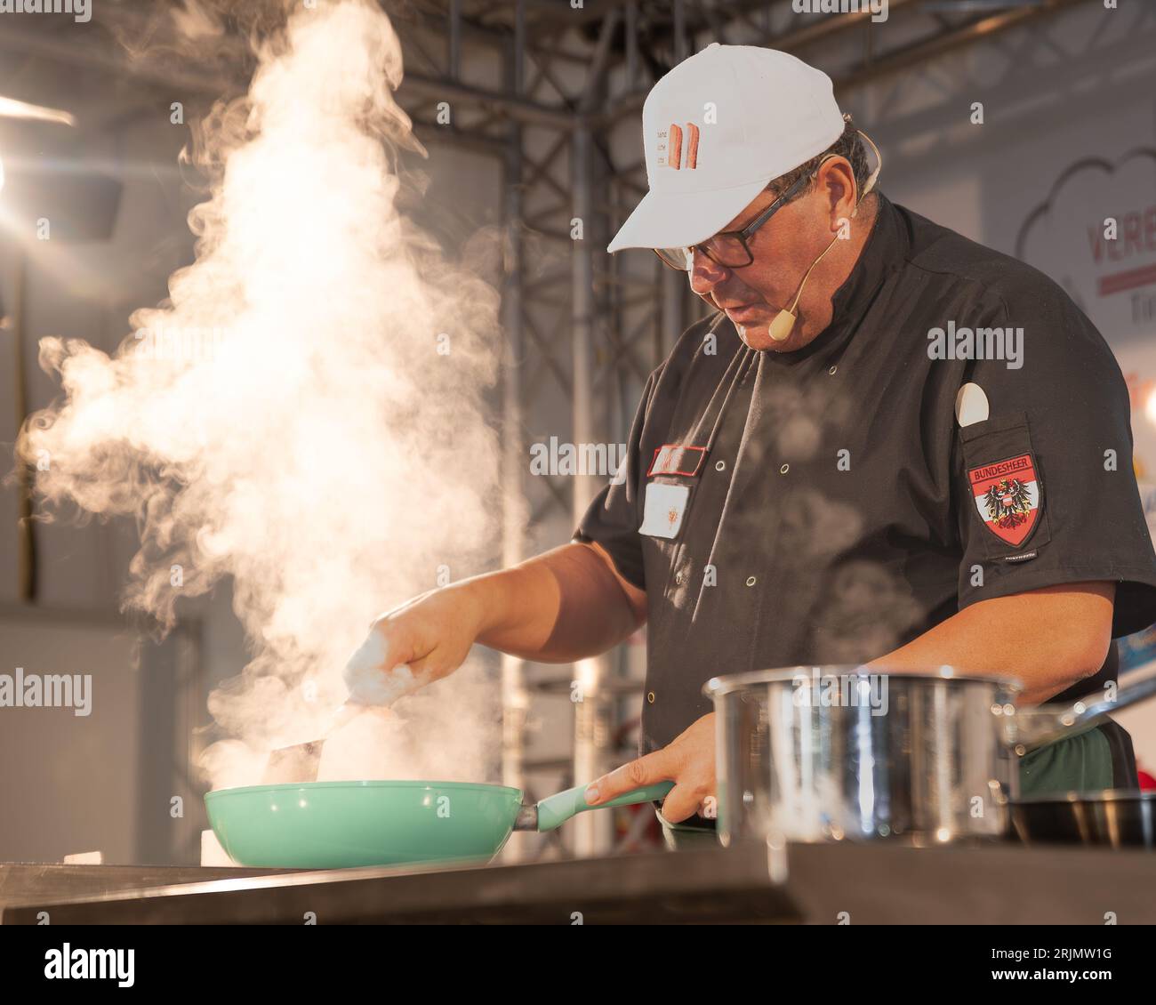 A chef is standing at a stovetop, cooking food in a pan suspended in ...
