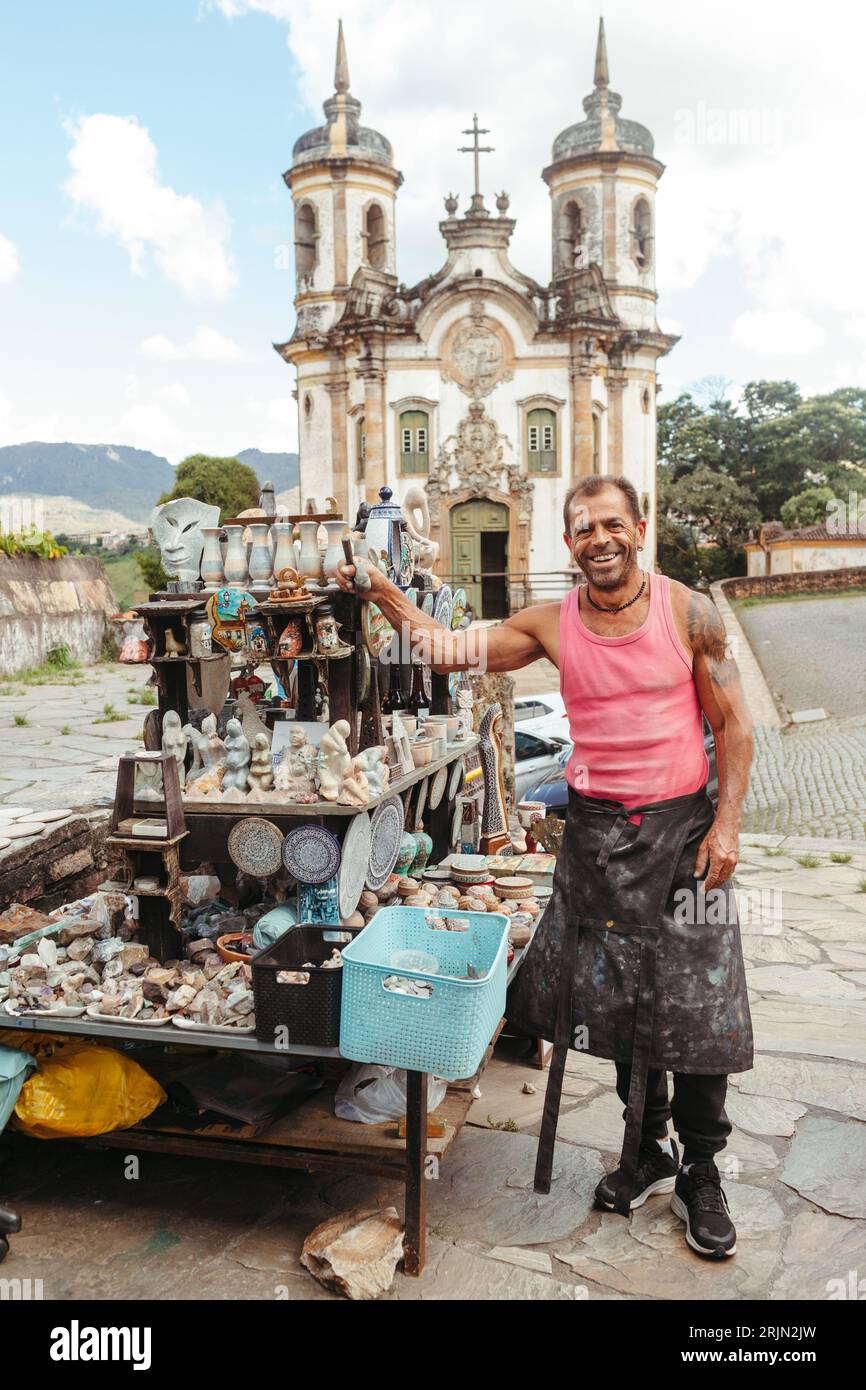 A mature man selling various antique objects on an outdoor stand in ...