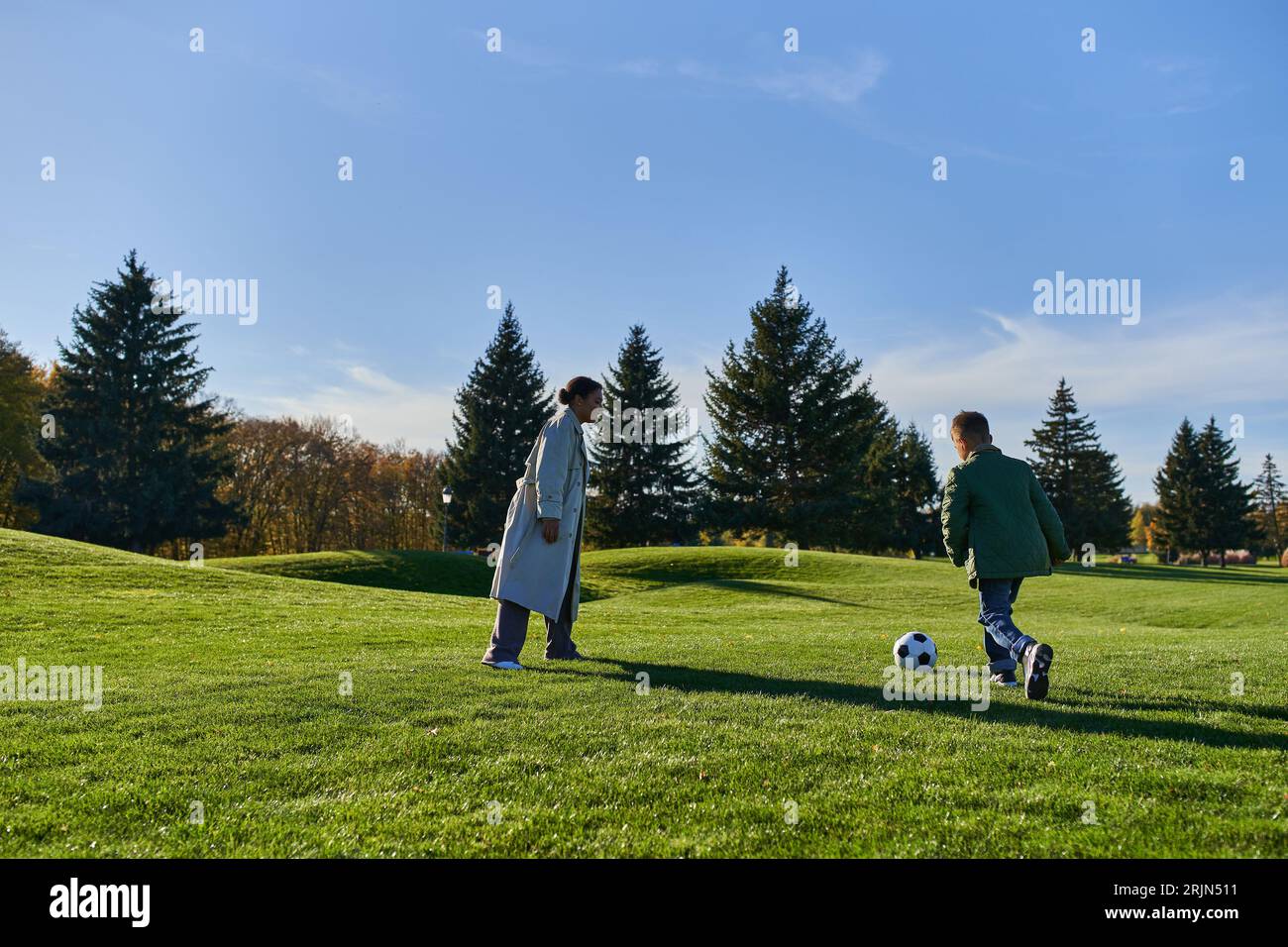 cheerful african american boy playing football with happy mother on green field, soccer, autumn ...