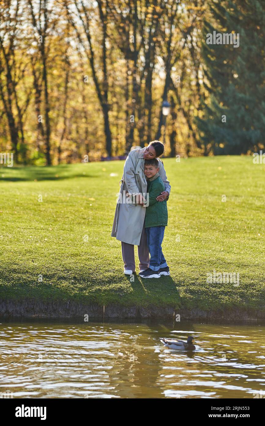 happy african american mother and son hugging near lake, duck, woman ...