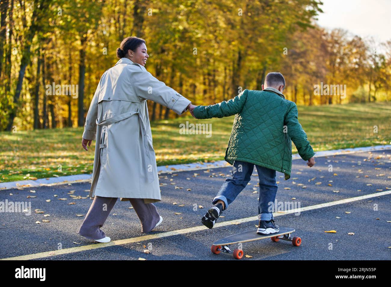 boy riding penny board and holding hands with cheerful mother, african ...