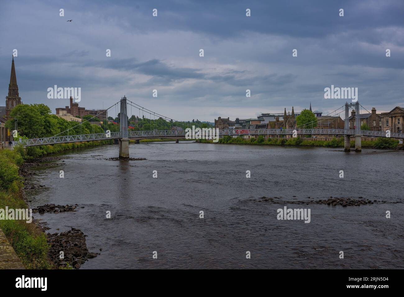 A walking bridge over the river Ness with a city background in ...