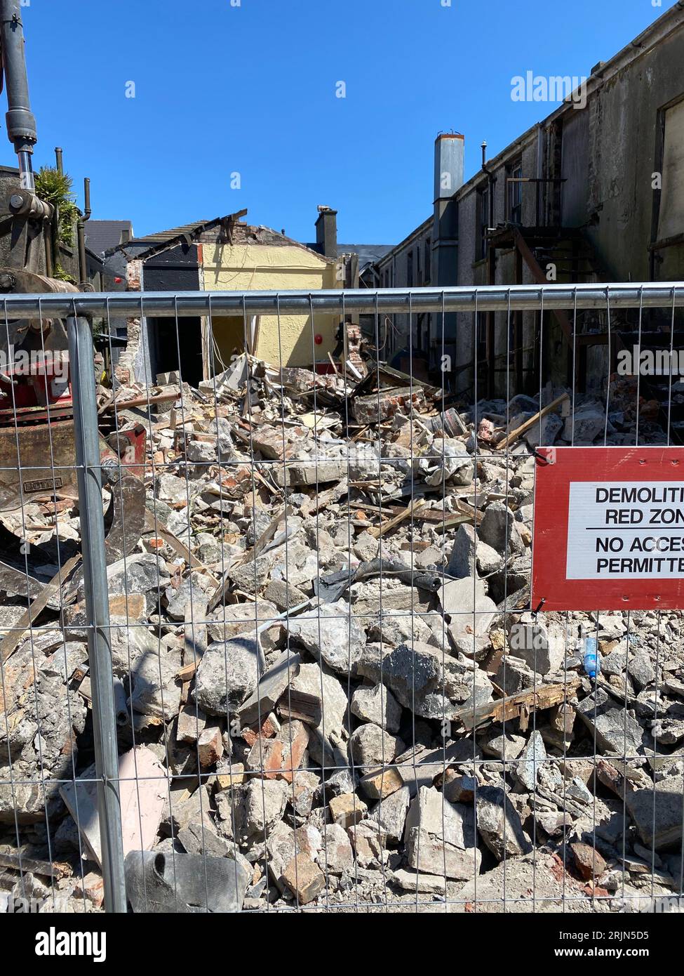 A demolition zone sign on a metal fence with stone debris in the ...