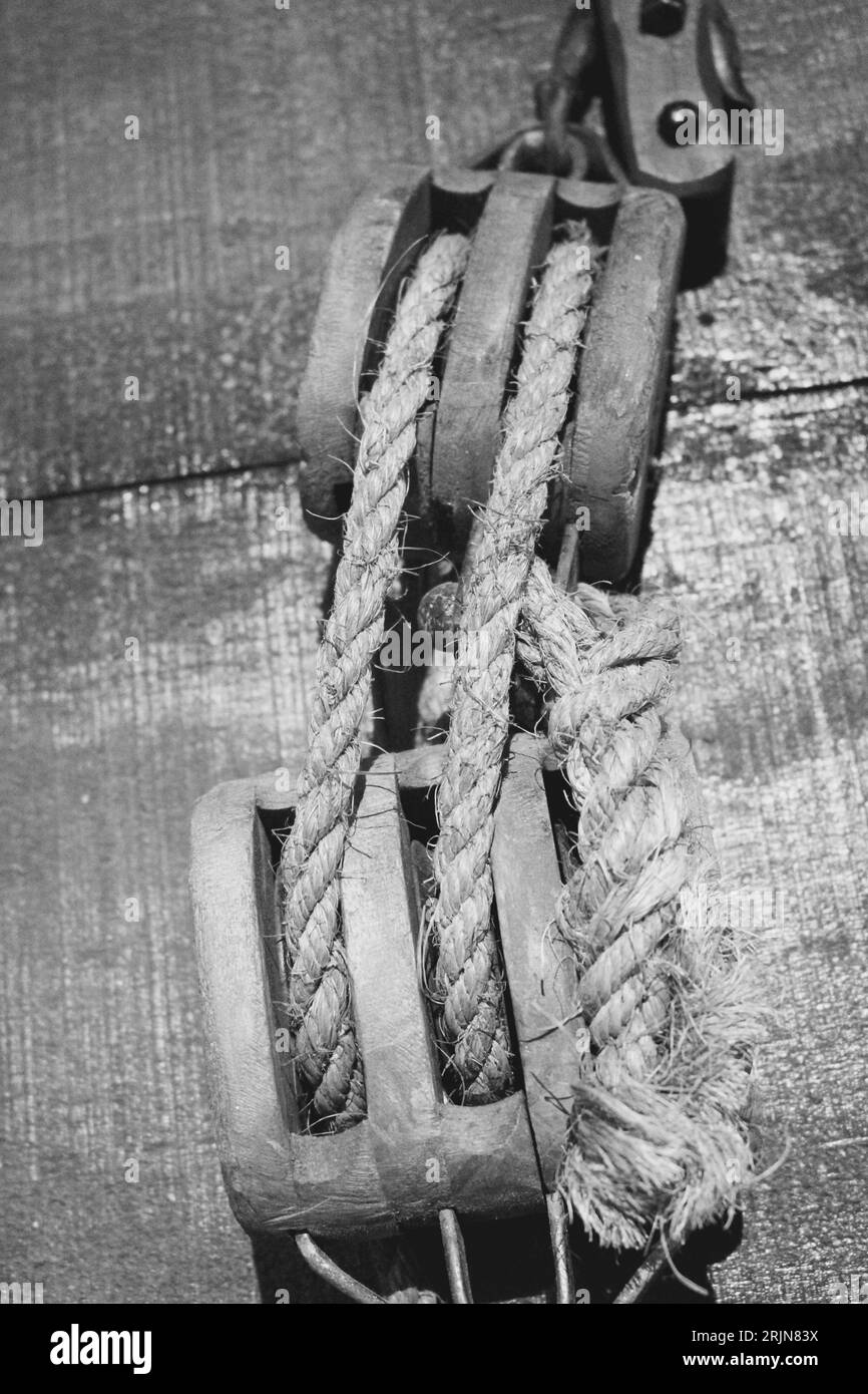 A close-up of ropes and pulleys on a traditional sailboat in grayscale ...