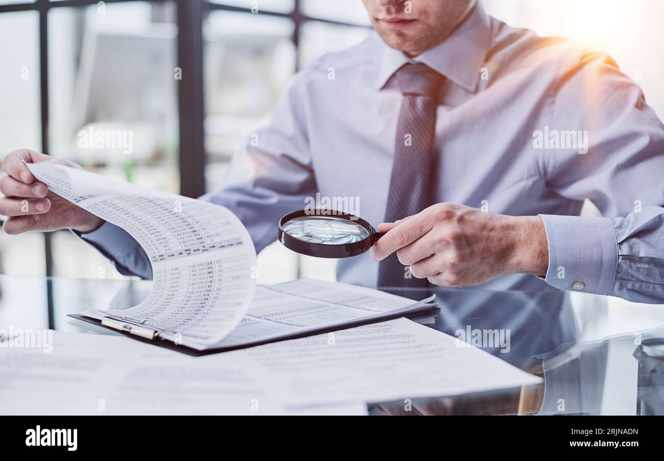 Businessman looking through a magnifying glass to documents Stock Photo ...