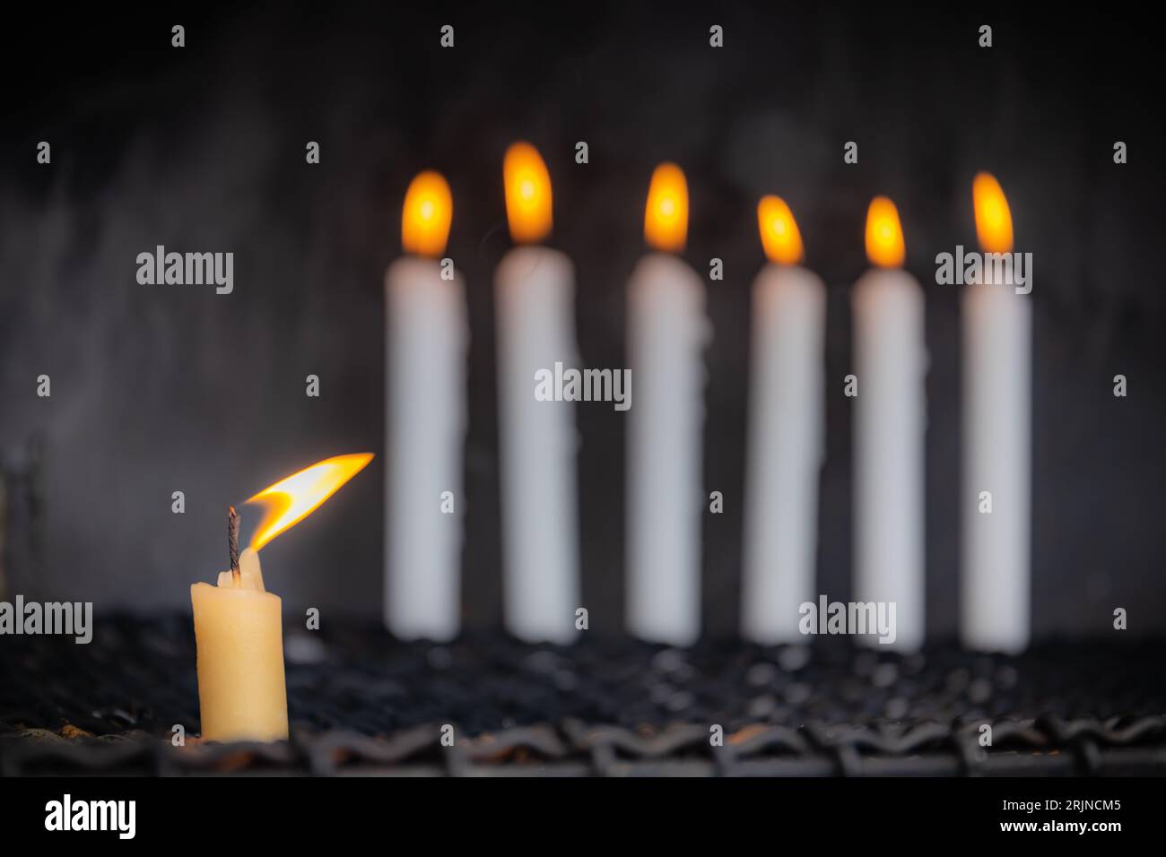 An image of seven lit candles arranged in a vertical line on a candle ...